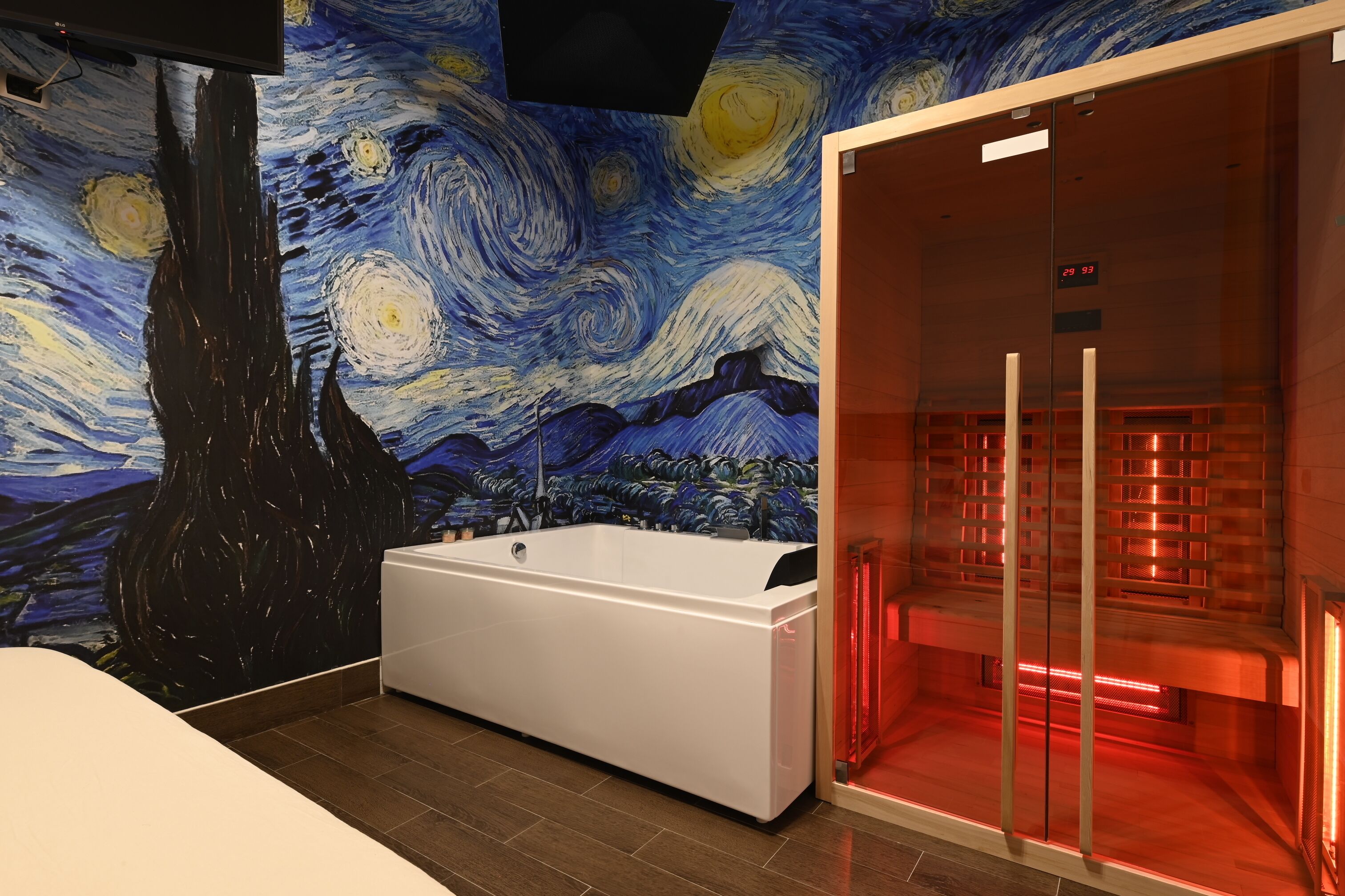 Uma casa de banho moderna com uma banheira branca, uma pintura grande de um céu noturno e uma área de sauna com iluminação vermelha.