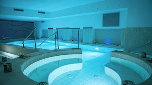 Piscina interior moderna com vários níveis e um elemento aquático central.