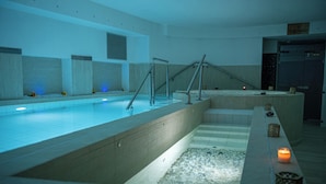Uma área interna de piscina moderna com superfície de água cristalina, um conjunto de escadas que levam a um nível superior e uma fileira de velas sobre um parapeito.