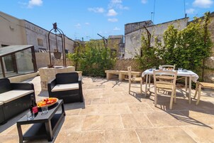 Uma área de pátio externa com piso de pedra, móveis de vime e uma mesa posta para refeições.