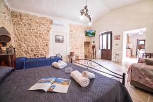 Quarto de hotel com parede de pedra, uma cama com uma revista, TV e vista para o exterior.