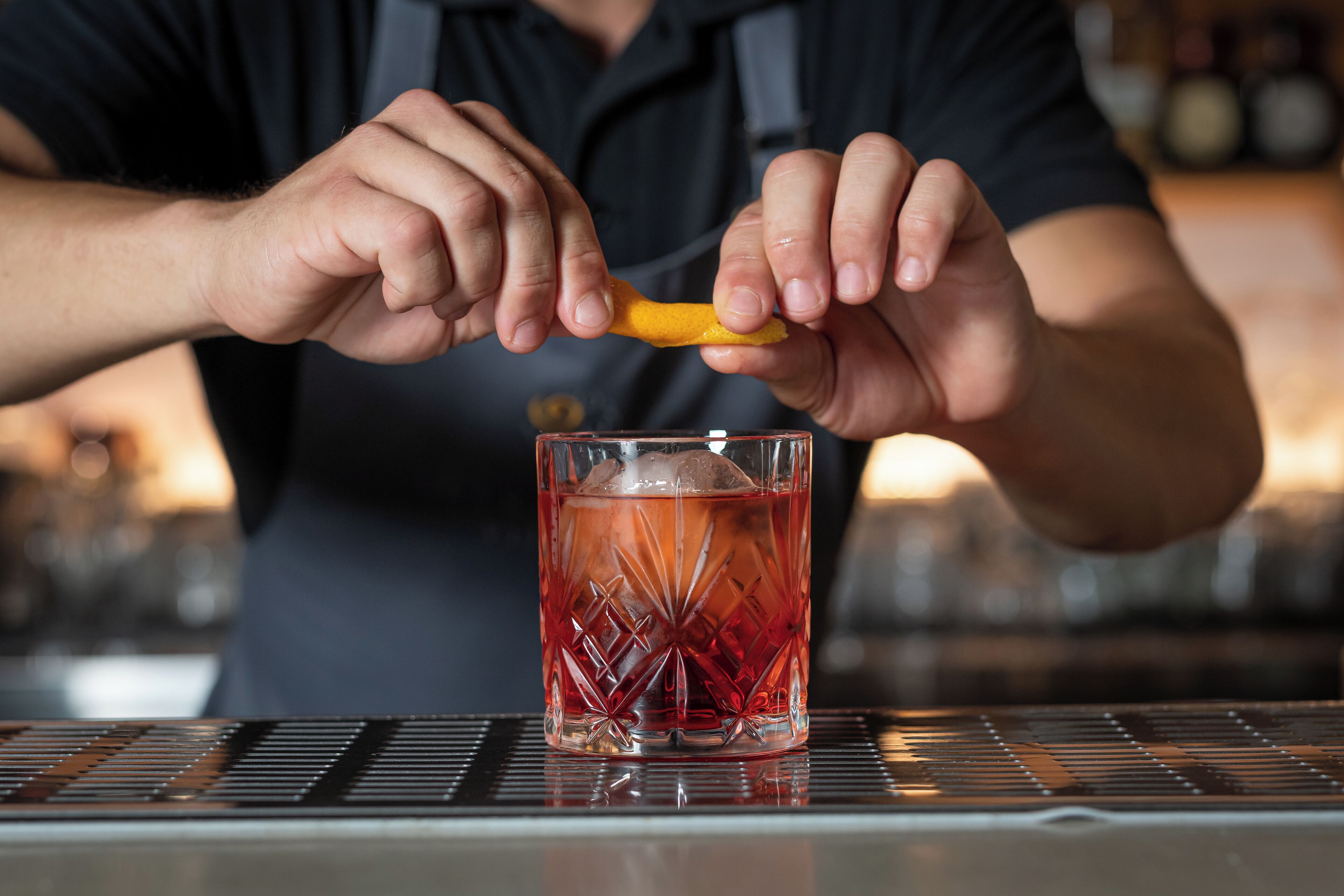 Um bartender espremendo um limão numa taça com bebida vermelha.