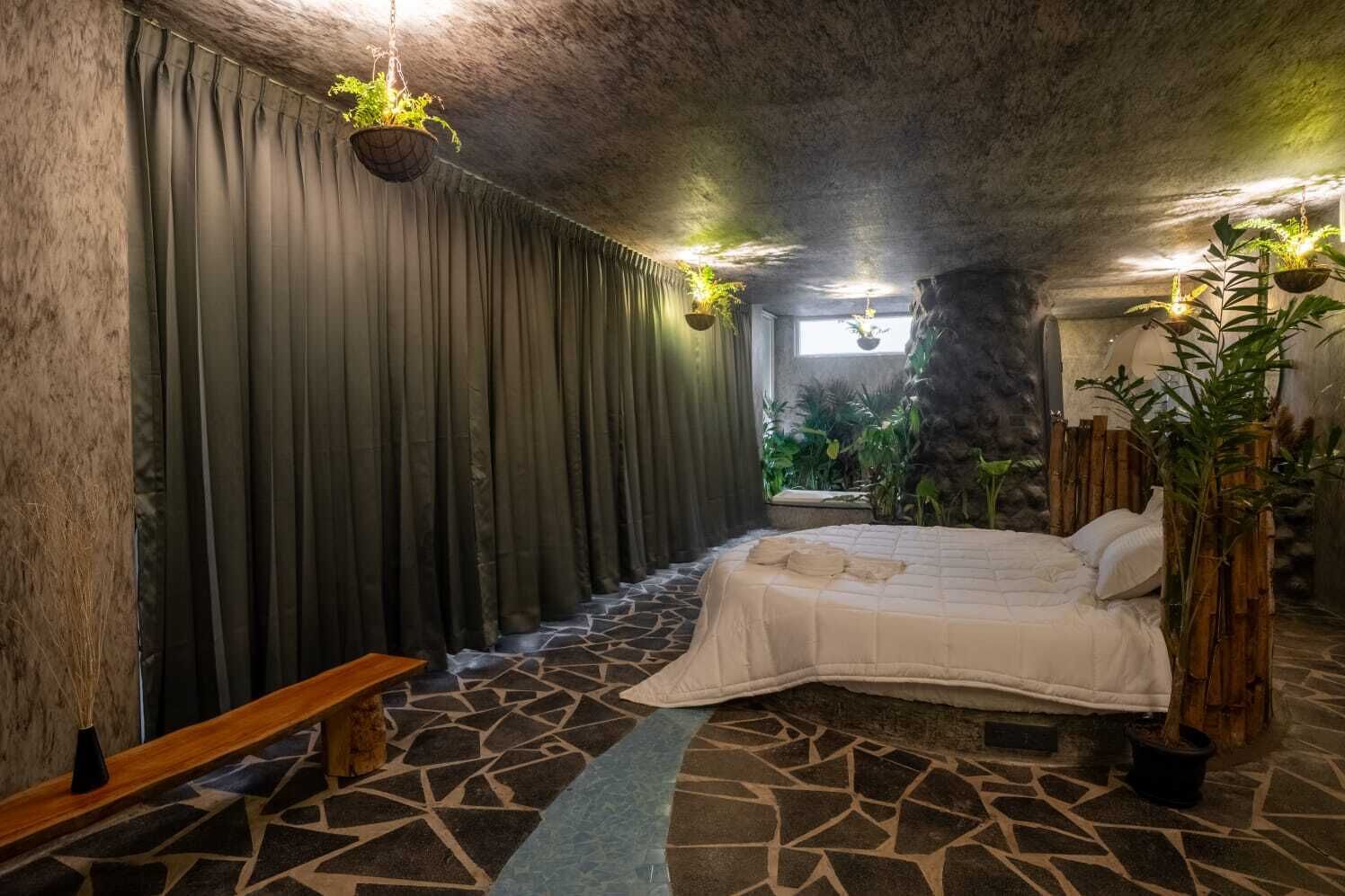 Quarto com cama, um banco e chão de pedra.