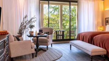 Quarto de hotel com cama, área de estar com mesa, planta em vaso e vista para o exterior.