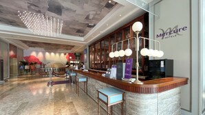 Uma área de recepção de hotel com balcão de mármore, banquetas, um lustre grande e uma placa na parede para Mercure Hotels.