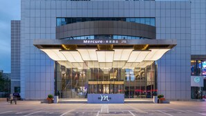 Uma entrada de hotel moderna com fachada de vidro, uma placa chamativa e uma área de estacionamento.