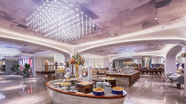 Um hall de hotel luxuoso com uma recepção de mármore, um grande candelabro e uma área de buffet.