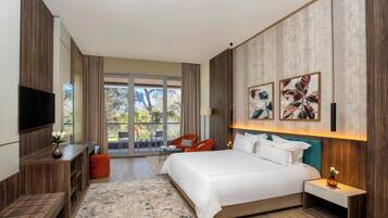 Quarto de hotel moderno com uma cama grande, televisão de tela plana, escrivaninha e área de estar com vista para o exterior.