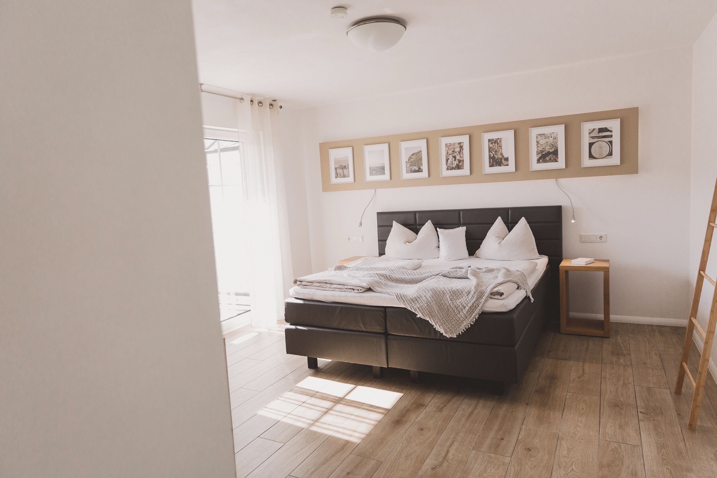 Quarto com cama, mesa de cabeceira, piso de madeira e janela com cortinas.