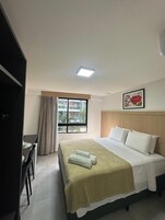 Quarto de hotel com cama, escrivaninha e janela com cortinas.