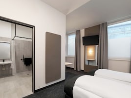Quarto de hotel com cama, banheiro, televisão e janela com cortinas.