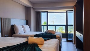 Quarto de hotel moderno com duas camas, uma janela grande e vista para o exterior.