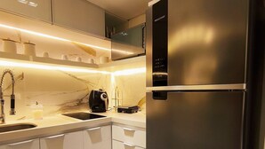 Uma cozinha moderna com geladeira de aço inoxidável, armários brancos, bancada de mármore e iluminação sob os armários.