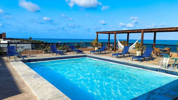 Piscina no terraço com cadeiras azuis e vista para o oceano.