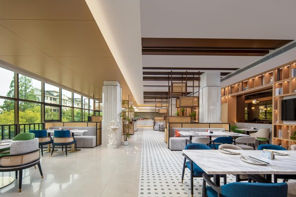 Um restaurante moderno com tetos altos, grandes janelas e uma área de jantar central com mesas e cadeiras.