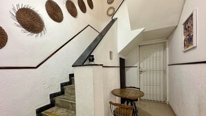 Uma escadaria com corrimão preto, uma mesa redonda com duas cadeiras e uma porta com portão de metal.