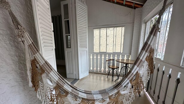 Uma rede em um quarto amplo com varanda, paredes brancas e vista para o exterior.