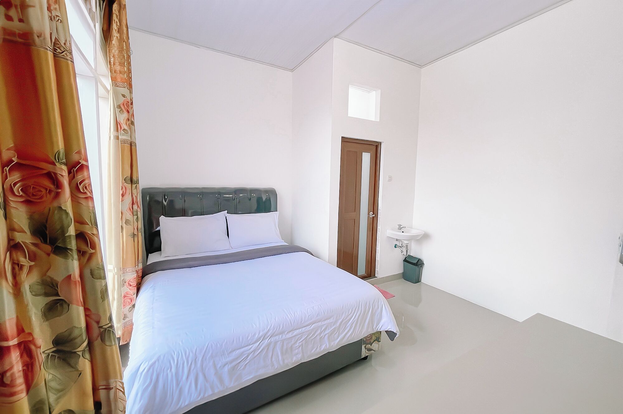 Um quarto com cama, porta de madeira, pequena janela e mesa de cabeceira com abajur.