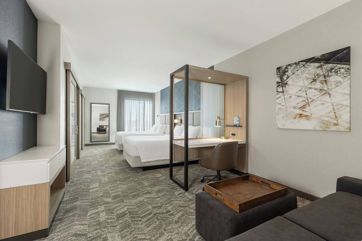 Quarto de hotel moderno com uma cama grande, uma escrivaninha, uma cadeira, uma TV e um quadro na parede.