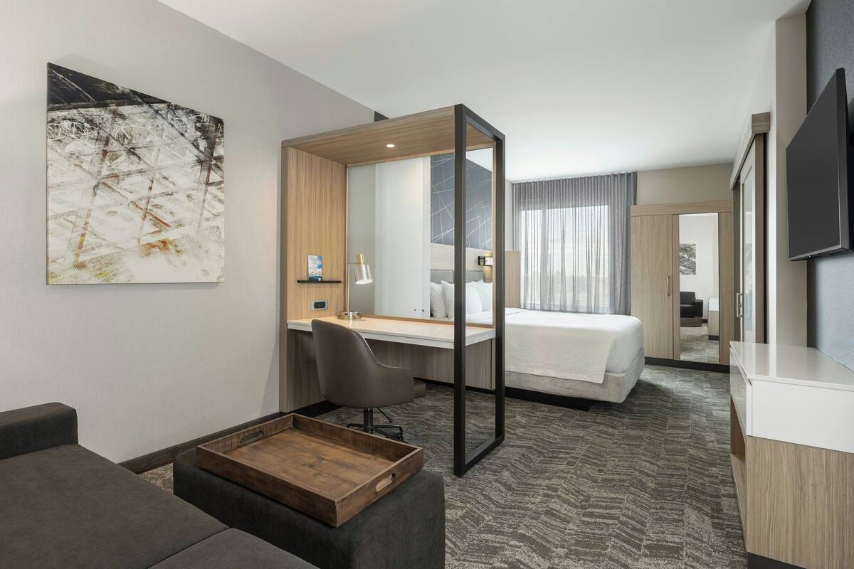 Quarto de hotel moderno com cama, escrivaninha e área de estar.