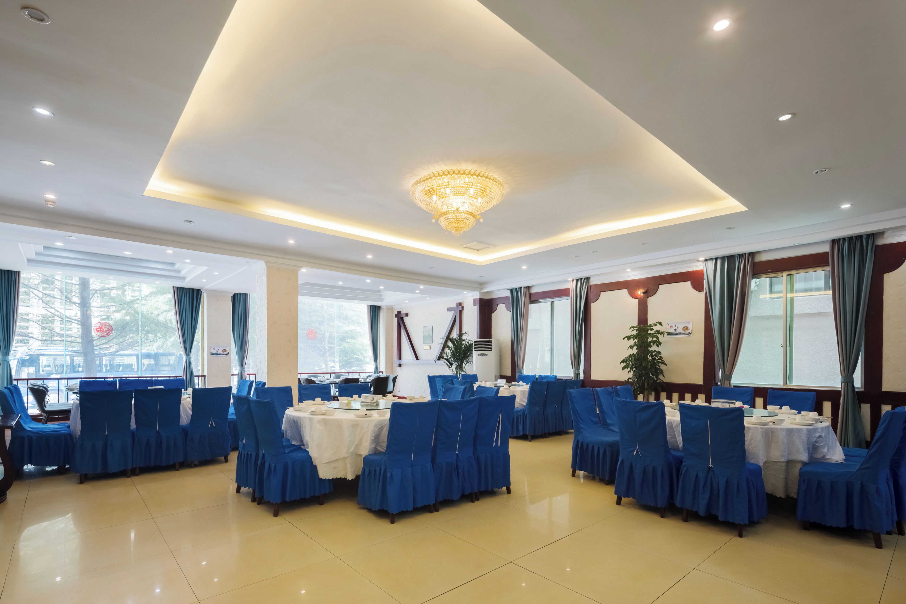 Uma sala de banquetes com mesas postas para refeições, cadeiras azuis e um lustre.