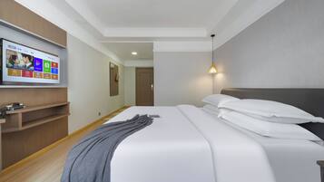 Quarto de hotel com cama, televisão fixada na parede, prateleira de madeira e porta que dá para outro quarto.