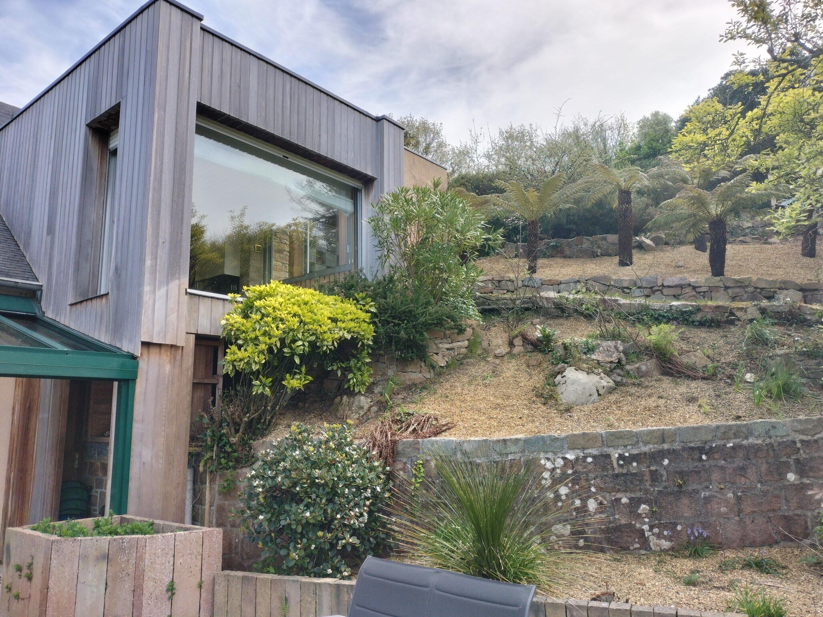 Uma casa moderna com uma grande janela de vidro, um deck de madeira e um muro de suporte de pedra.