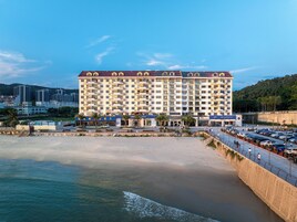 Um hotel com vários andares e vista para a praia, situado perto de um parque de estacionamento e de um calçadão.