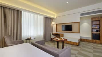 Quarto de hotel com cama, duas poltronas, uma mesinha, televisão e minibar.