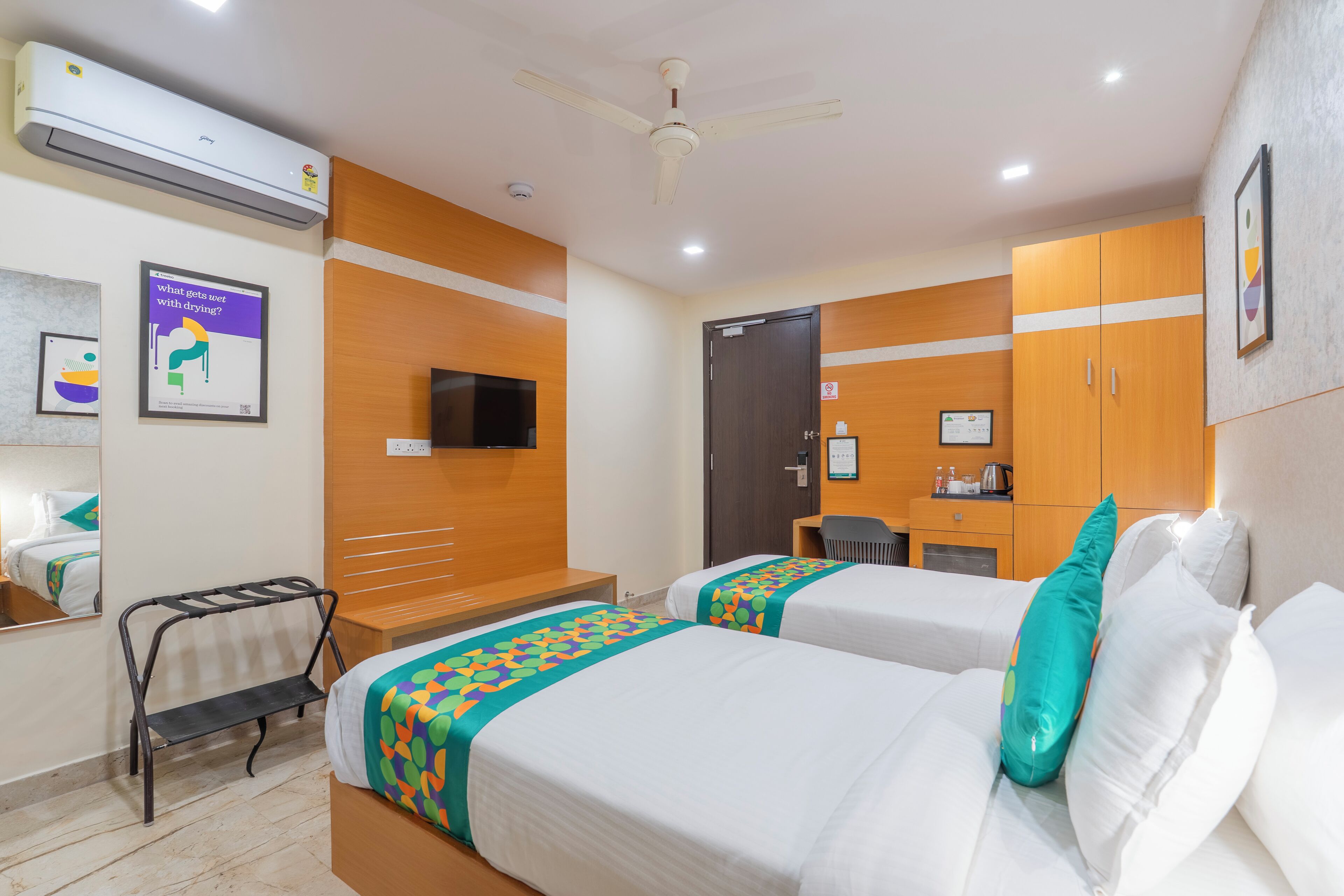 Quarto de hotel com duas camas, uma escrivaninha, uma cadeira, televisão e cozinha compacta.