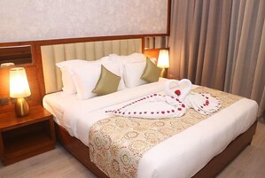 Quarto de hotel bem arrumado, com cama, almofadas, abajur e uma decoração de toalhas.
