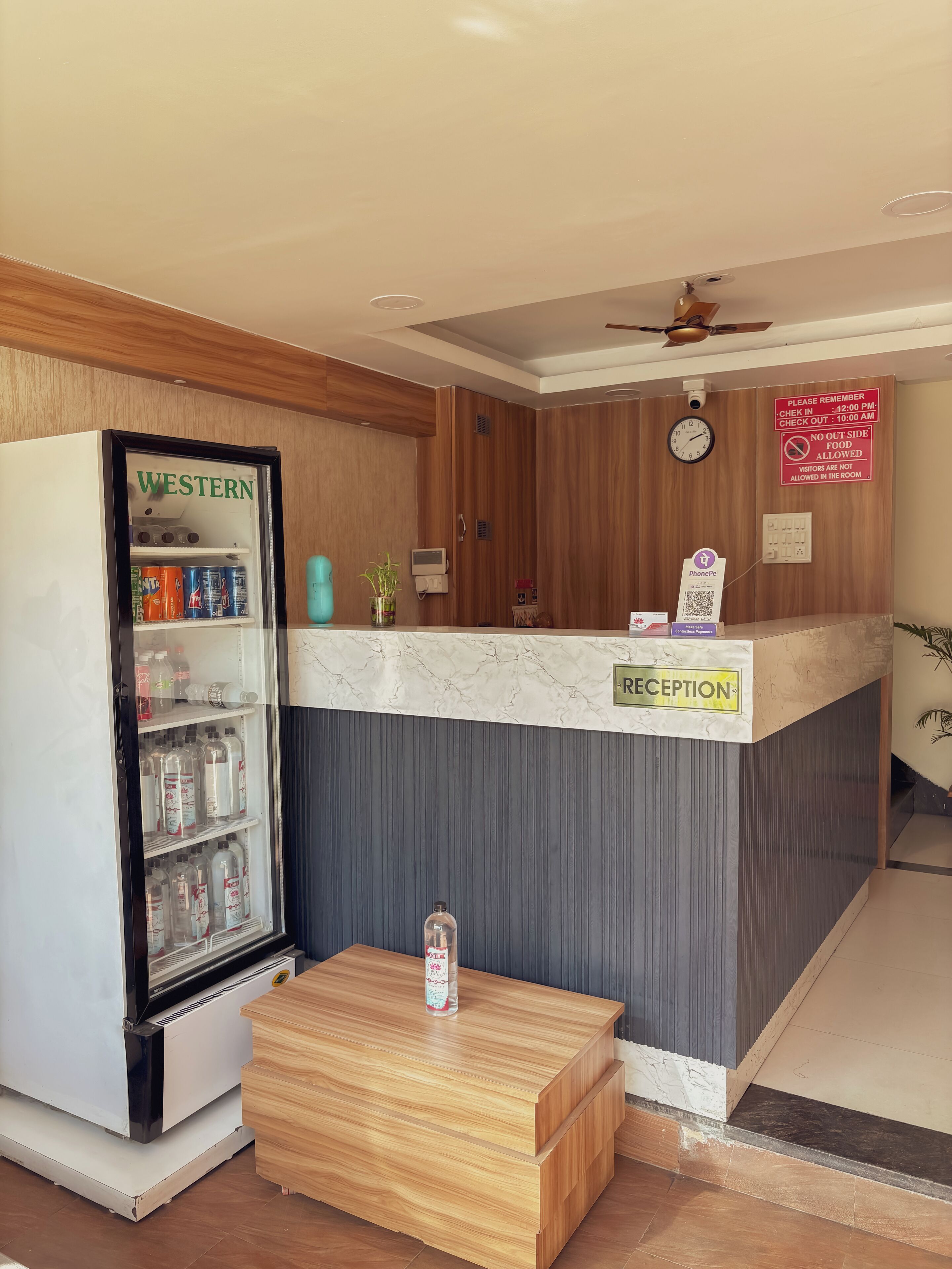 Bancada de recepção com uma placa indicando 'Reception', uma placa 'PhonePe', um relógio e uma placa com a mensagem 'Não é permitido trazer comida de fora'.