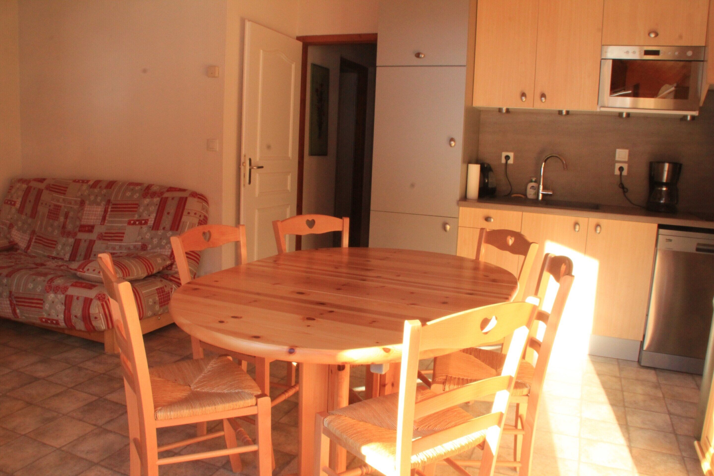 Uma cozinha acolhedora com uma mesa e cadeiras de madeira, um sofá e uma geladeira.