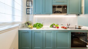 Uma cozinha com armários verde-água, micro-ondas, forno e pia com legumes frescos.