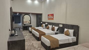 Quarto de hotel com três camas, uma escrivaninha, um espelho e um quadro na parede.