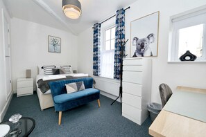 Quarto moderno com cama, uma cadeira azul, escrivaninha e janela com cortinas.