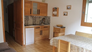 Uma cozinha compacta com armários de madeira, painel de azulejos e uma pequena mesa de jantar com toalha de mesa florida.
