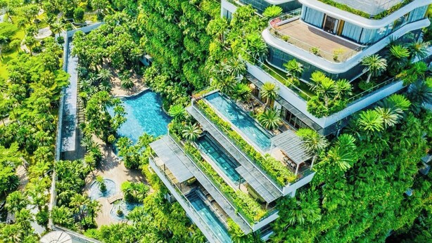Vista aérea de um resort moderno com várias piscinas, cercado por vegetação exuberante e palmeiras.