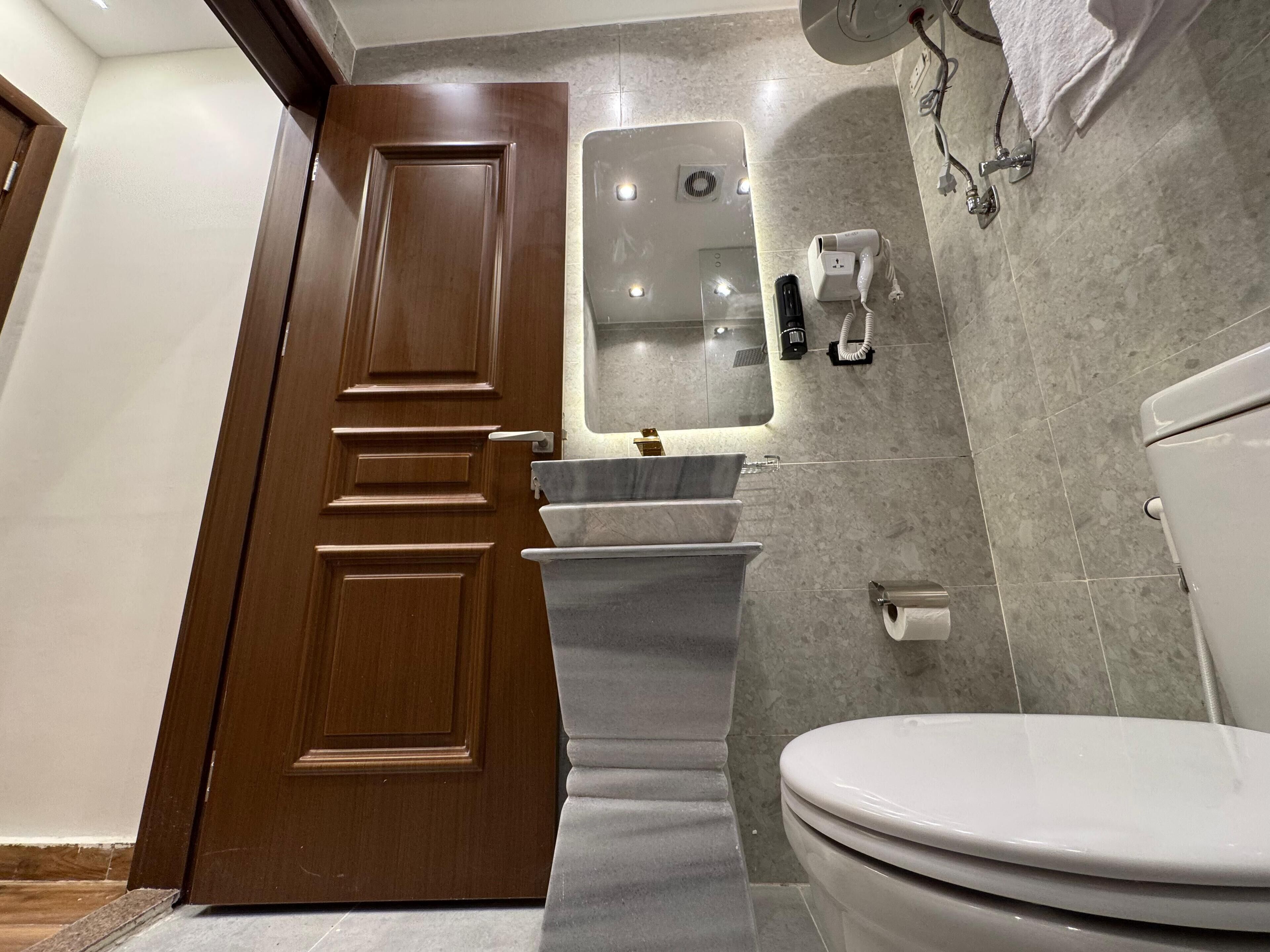 Um banheiro com porta de madeira, pia com espelho, vaso sanitário e porta-toalhas.