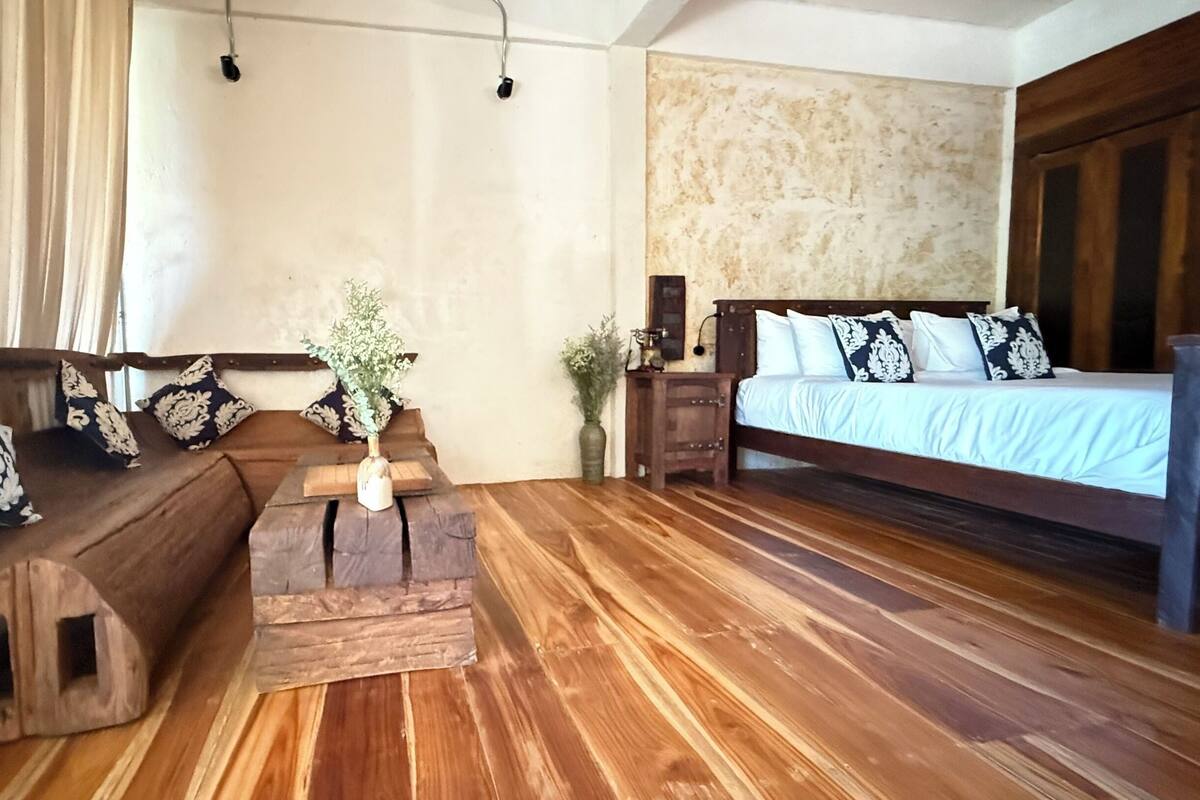 Quarto com piso de madeira, uma cama, um sofá e uma mesinha com um vaso.