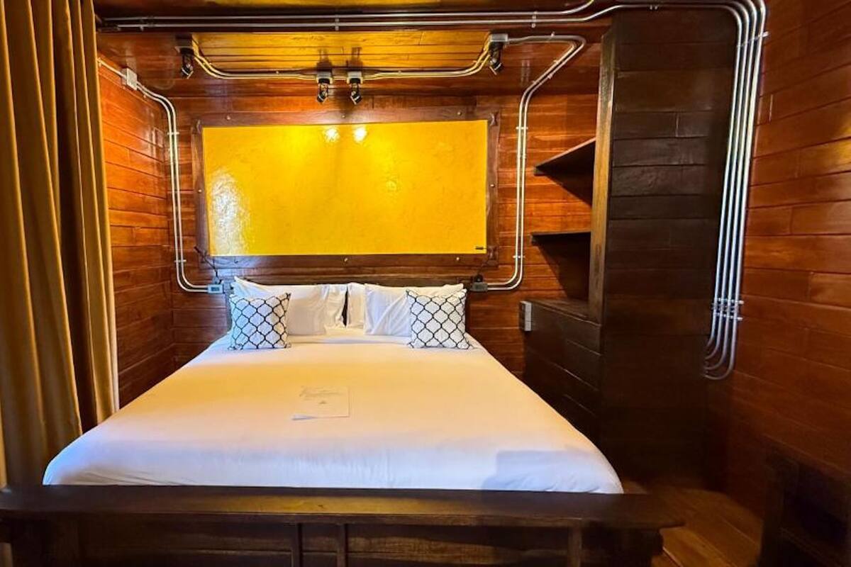 Um quarto de madeira com uma cama, uma janela com cortinas e uma lareira.