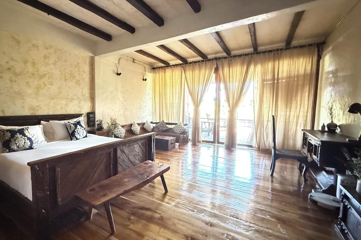 Quarto rústico com cama de madeira, banco e vista do exterior por grandes janelas.