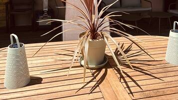 Uma mesa de madeira com um vaso de planta, duas lanternas brancas e uma cesta suspensa.