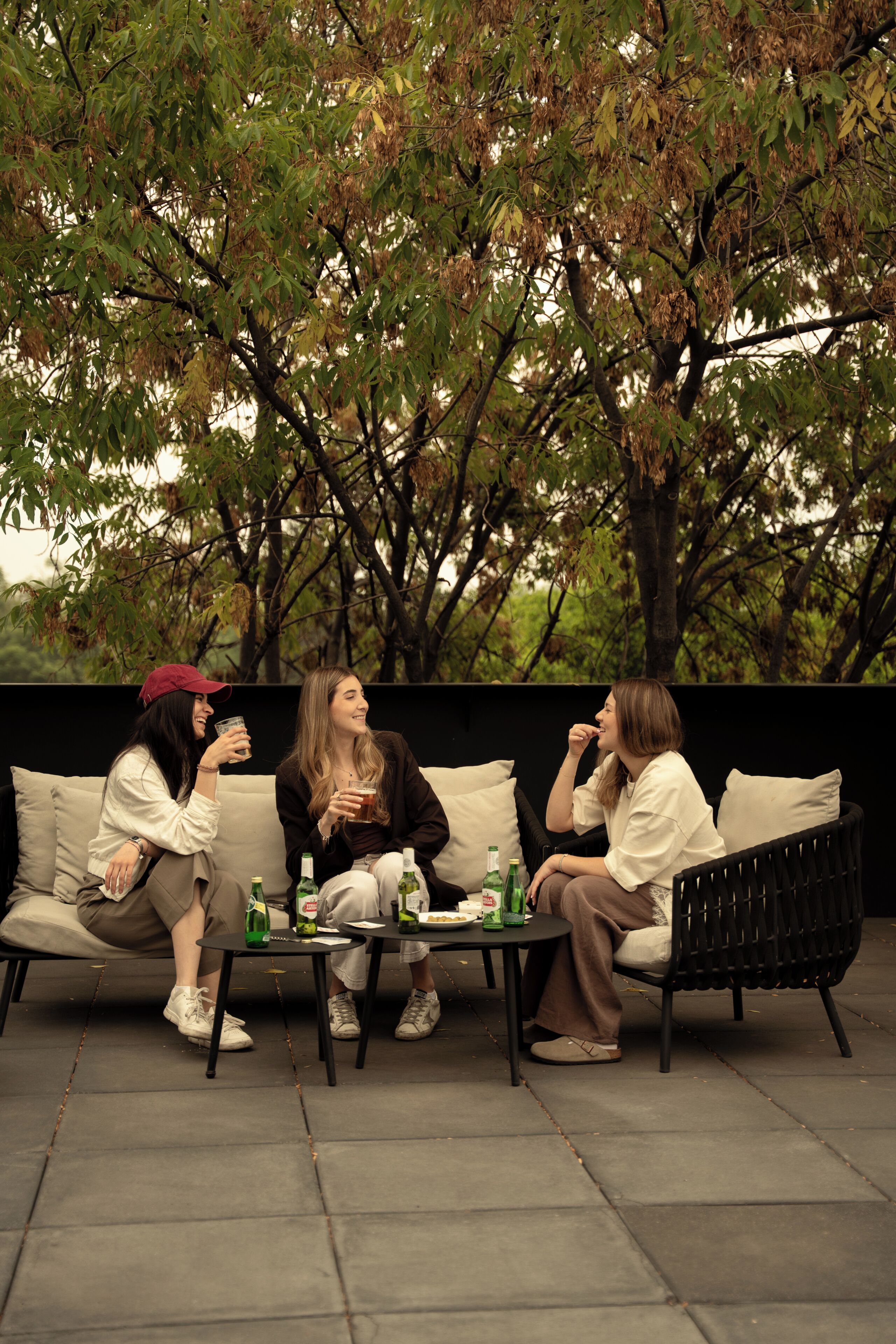 Três pessoas sentadas em um sofá e cadeiras ao ar livre, com uma mesa no meio.