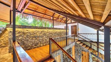 Uma escada de madeira com paredes de pedra e corrimão de metal, que leva a um andar superior com vista para o exterior.