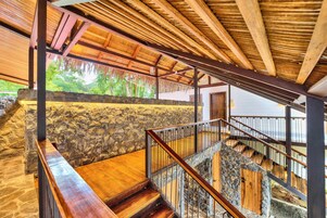 Uma escada de madeira com paredes de pedra e corrimão de metal, que leva a um andar superior com vista para o exterior.