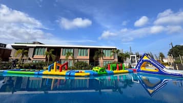 Piscina com estruturas infláveis e um edifício de hotel ao fundo.