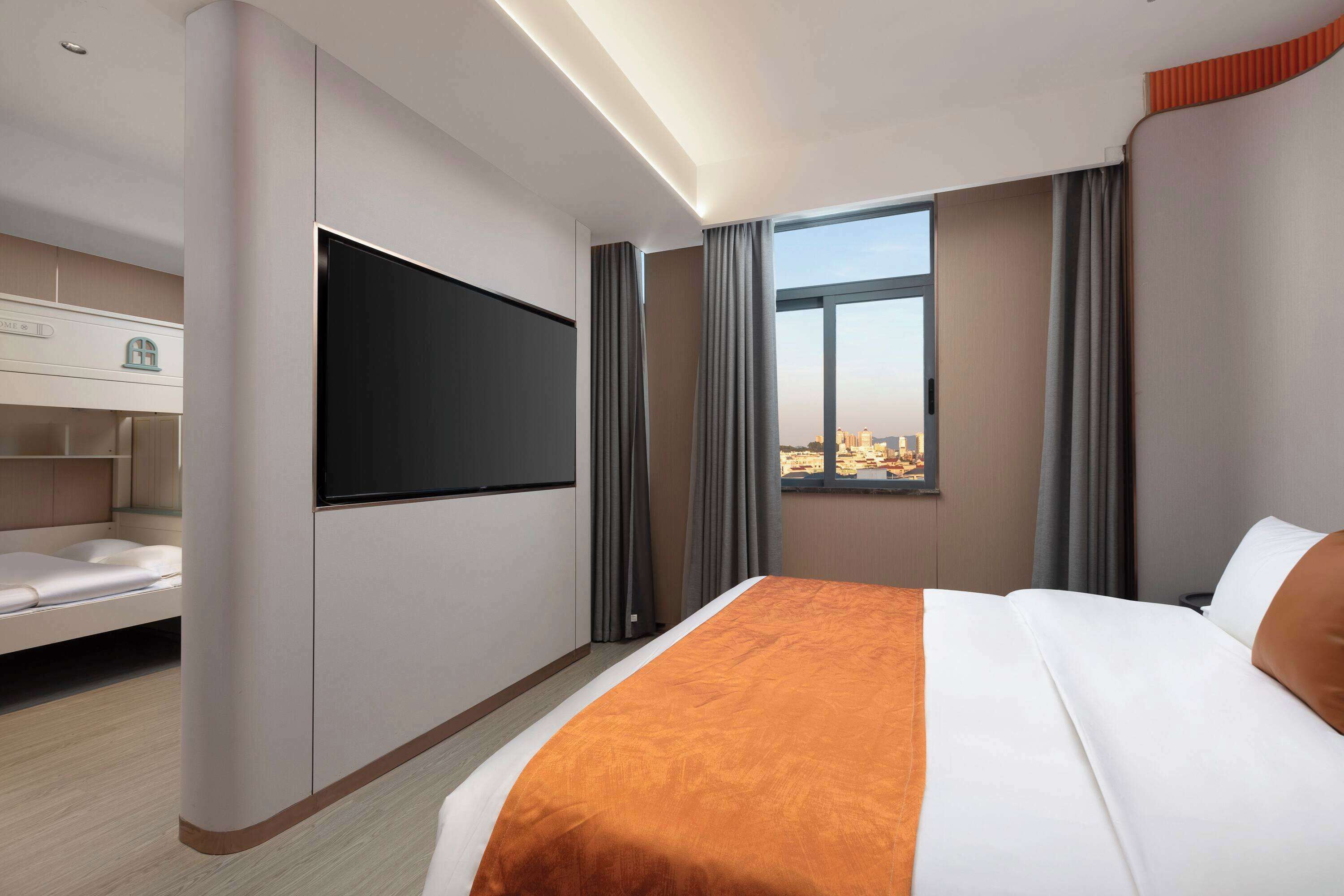 Quarto de hotel com cama, televisão, janela com vista para a cidade e escrivaninha com cadeira.