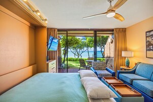 Quarto de hotel com cama, sofá, televisão e vista para o mar.