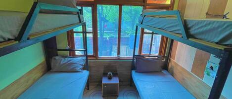 Quarto com beliches, uma mesinha e janela com vista para o verde.